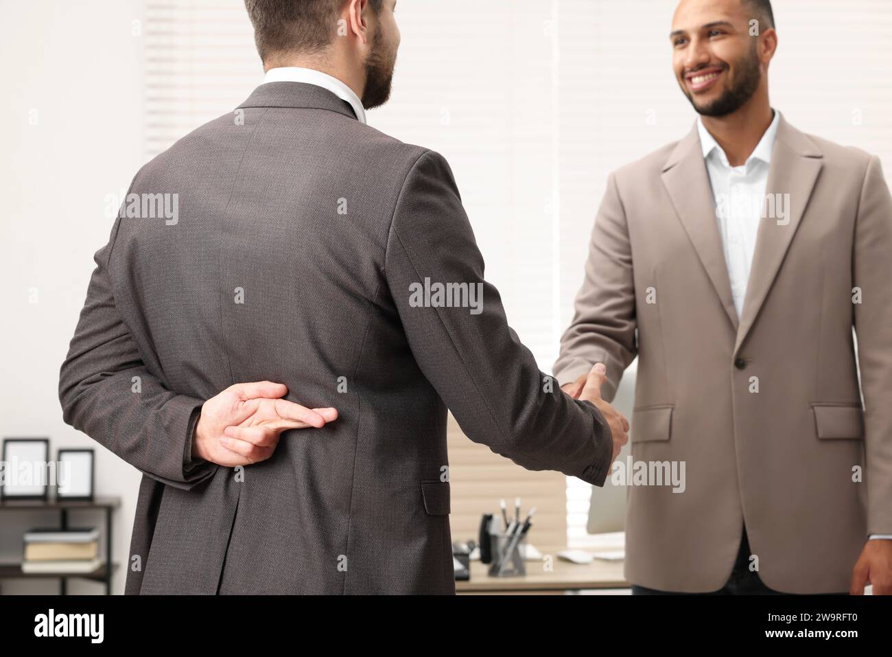 Employee crossing fingers behind his back while shaking hands with boss ...