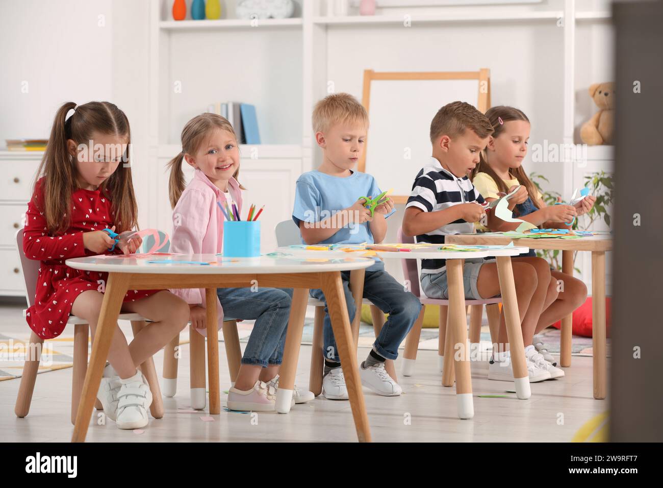 Group of cute little children making toys from color paper at desks in ...