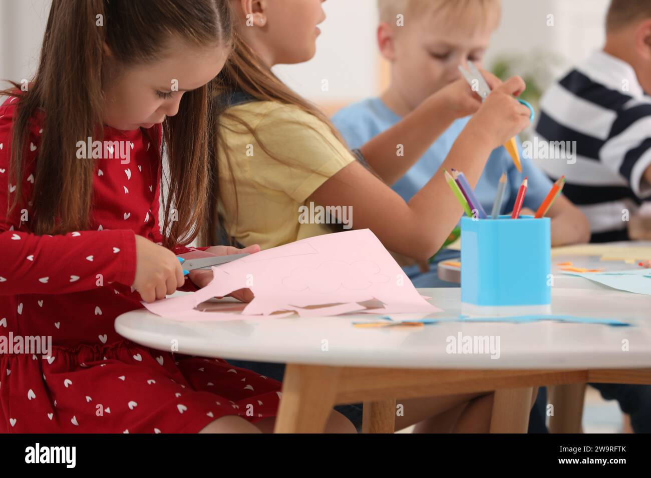 Group of cute little children making toys from color paper at desk in ...