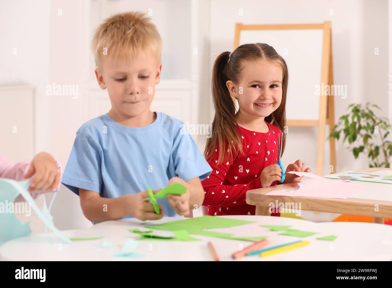 Cute little children cutting color paper with scissors at desk in ...
