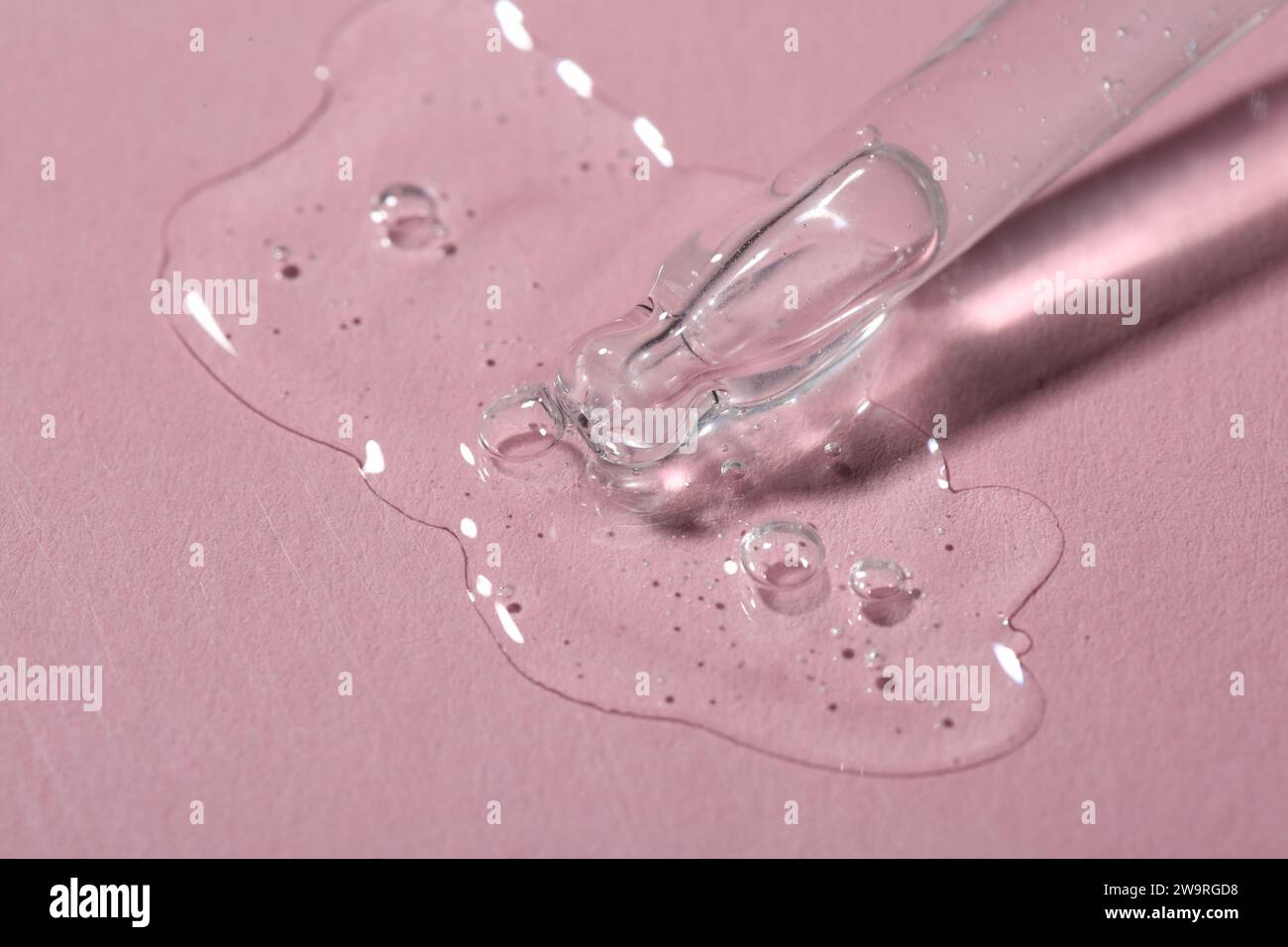 Dripping cosmetic serum from pipette onto pink background, macro view ...