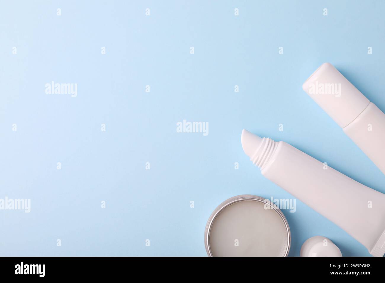Different lip balms on light blue background, flat lay. Space for text ...