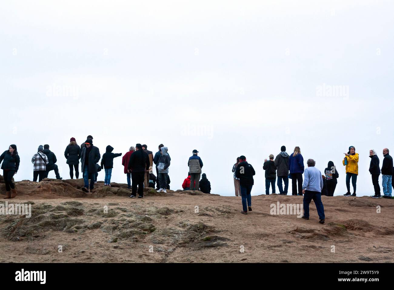 Crowds of people seen from behind standing at the edge of a cliff ...