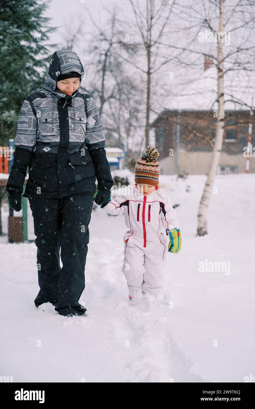 Mom and little girl walk holding hands through the snowdrifts under the ...