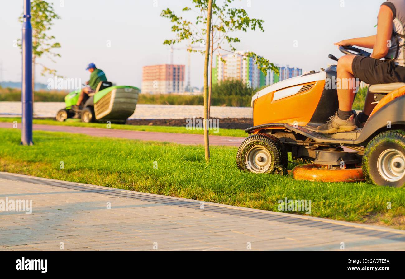 Workers drive lawn mowers tractors and mow the lawn in the park in the ...