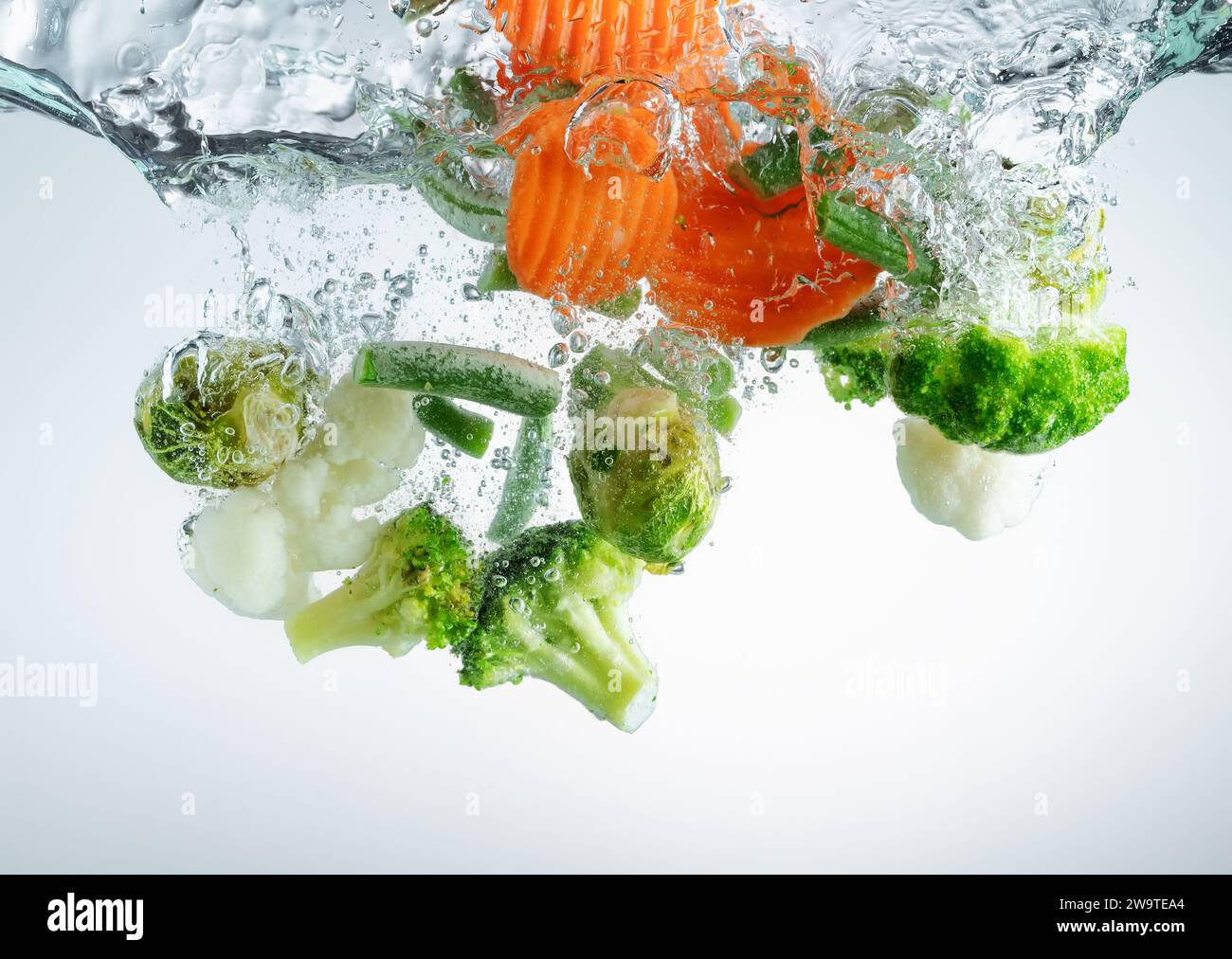 Vegetables falling into water with splashes and air bubbles. Cooking ...