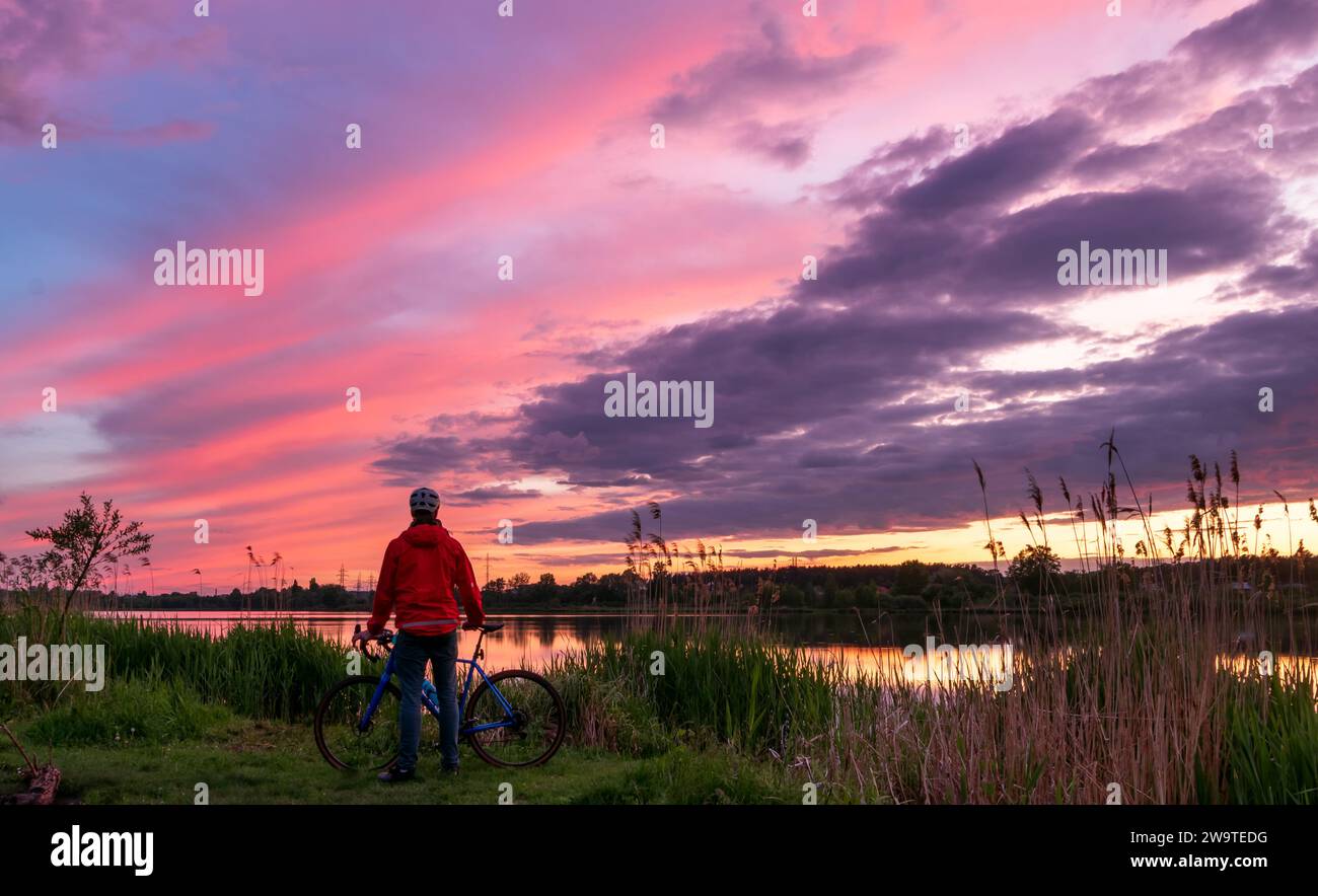 Cyclist on the coast of the river at sunset in summer. Landscape with ...
