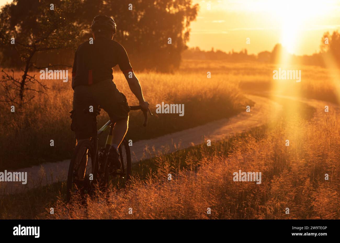 Cyclist riding a trail in a field on a gravel bike on a dramatic sunset ...