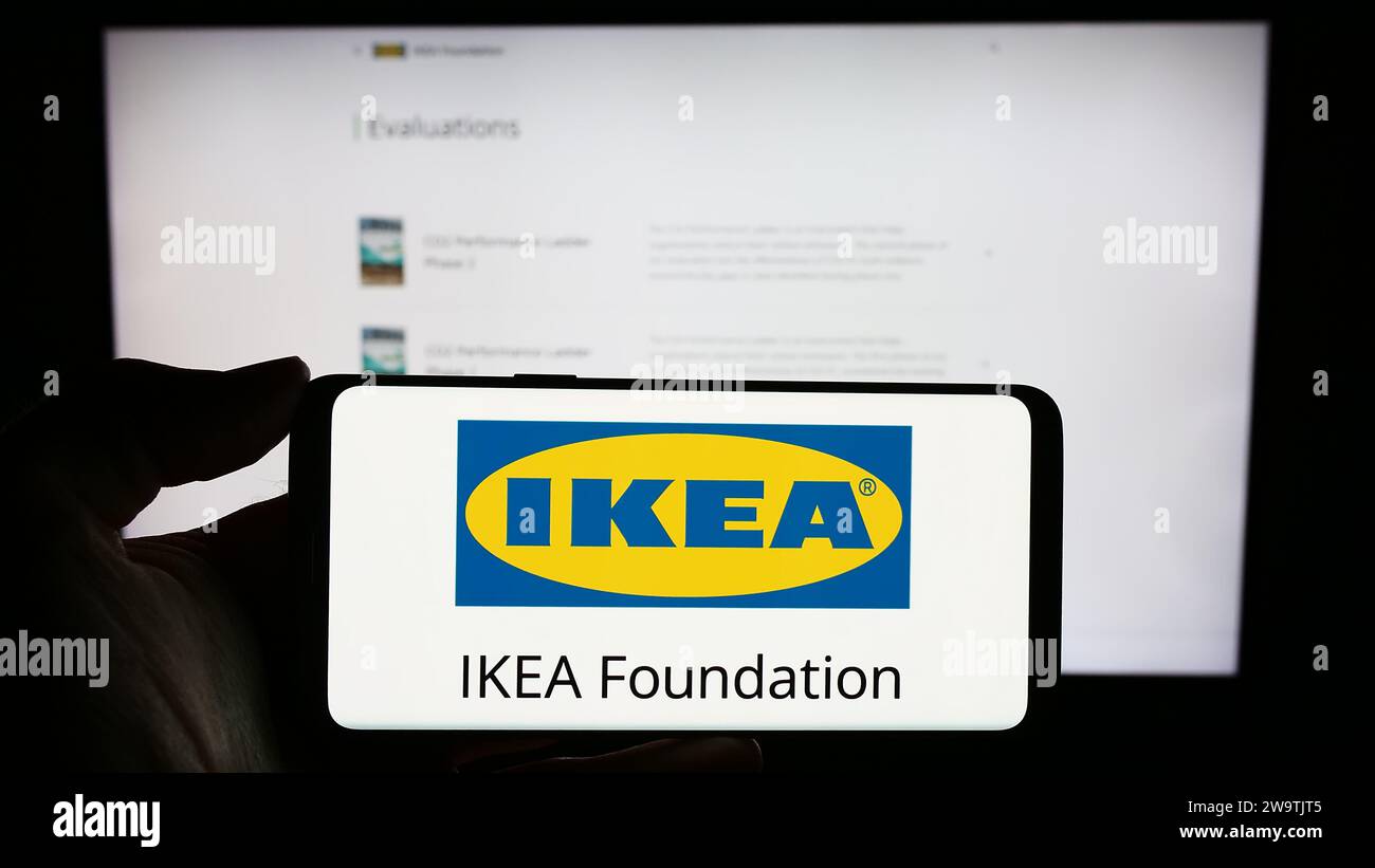 Person holding cellphone with logo of organization IKEA Foundation in front of webpage. Focus on ...