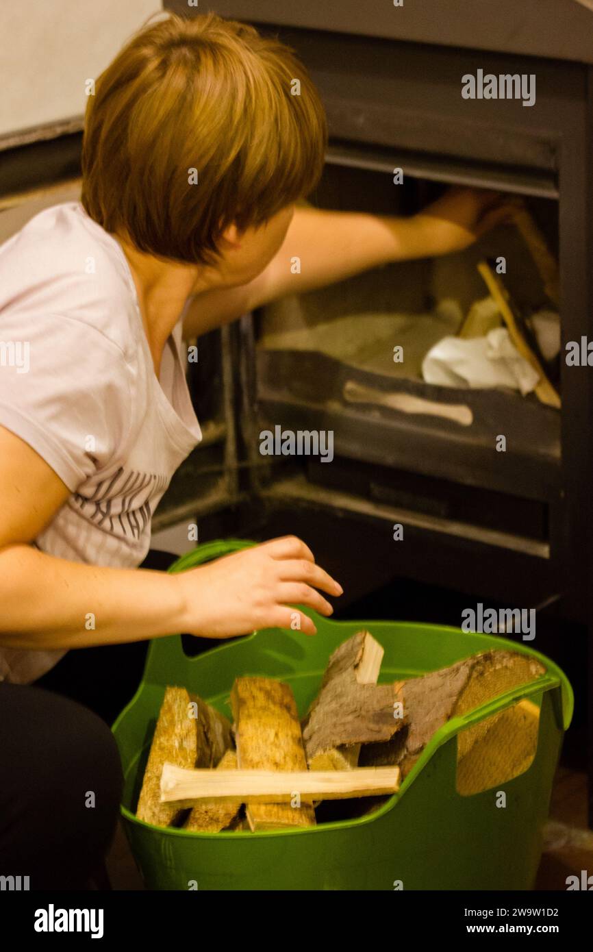 Woman making fire in fireplace. Basket with firewood in rural log ...