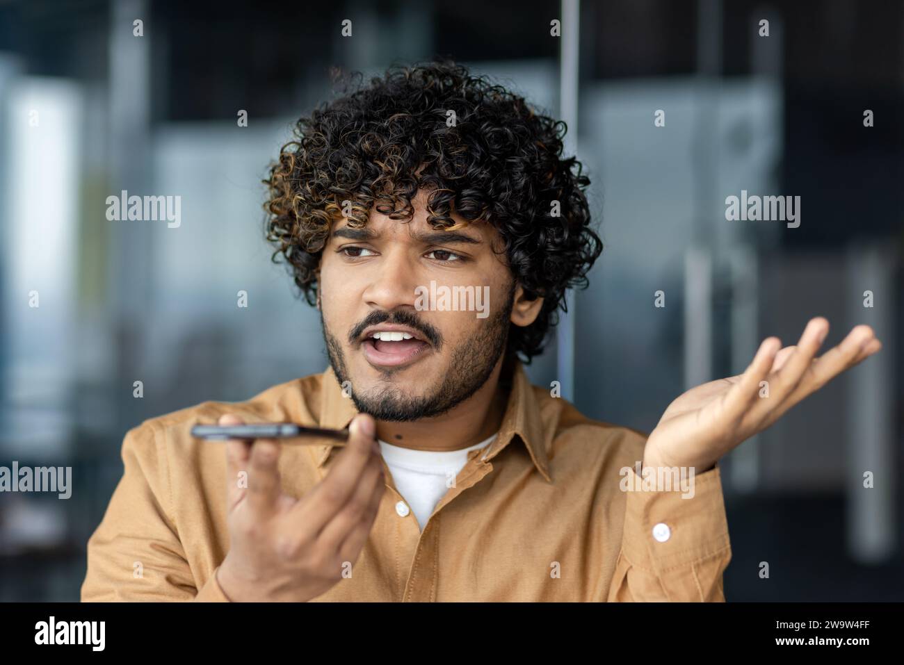 Close-up photo of worried and nervous young Indian man talking on speaker phone and using search ...
