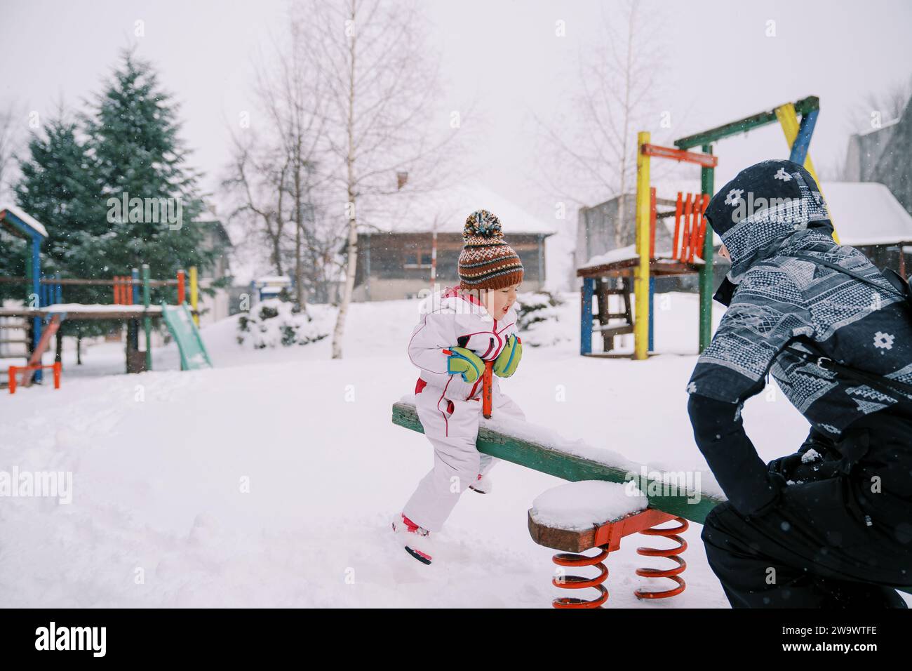 Mom and little girl ride on a snowy swing-balancer on a colorful ...