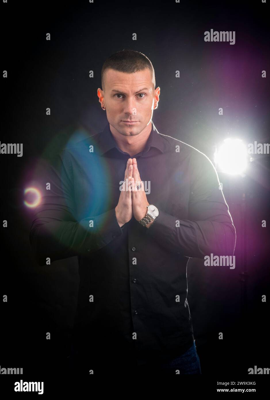 A man standing in front of a spotlight, with hands joined together ...