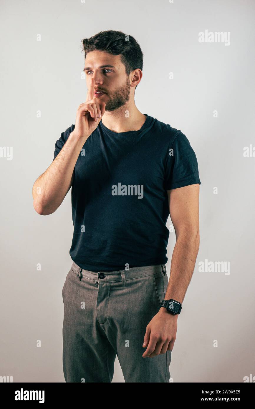 Hush. Young handsome man silencing you, saying shut up, in studio shot ...