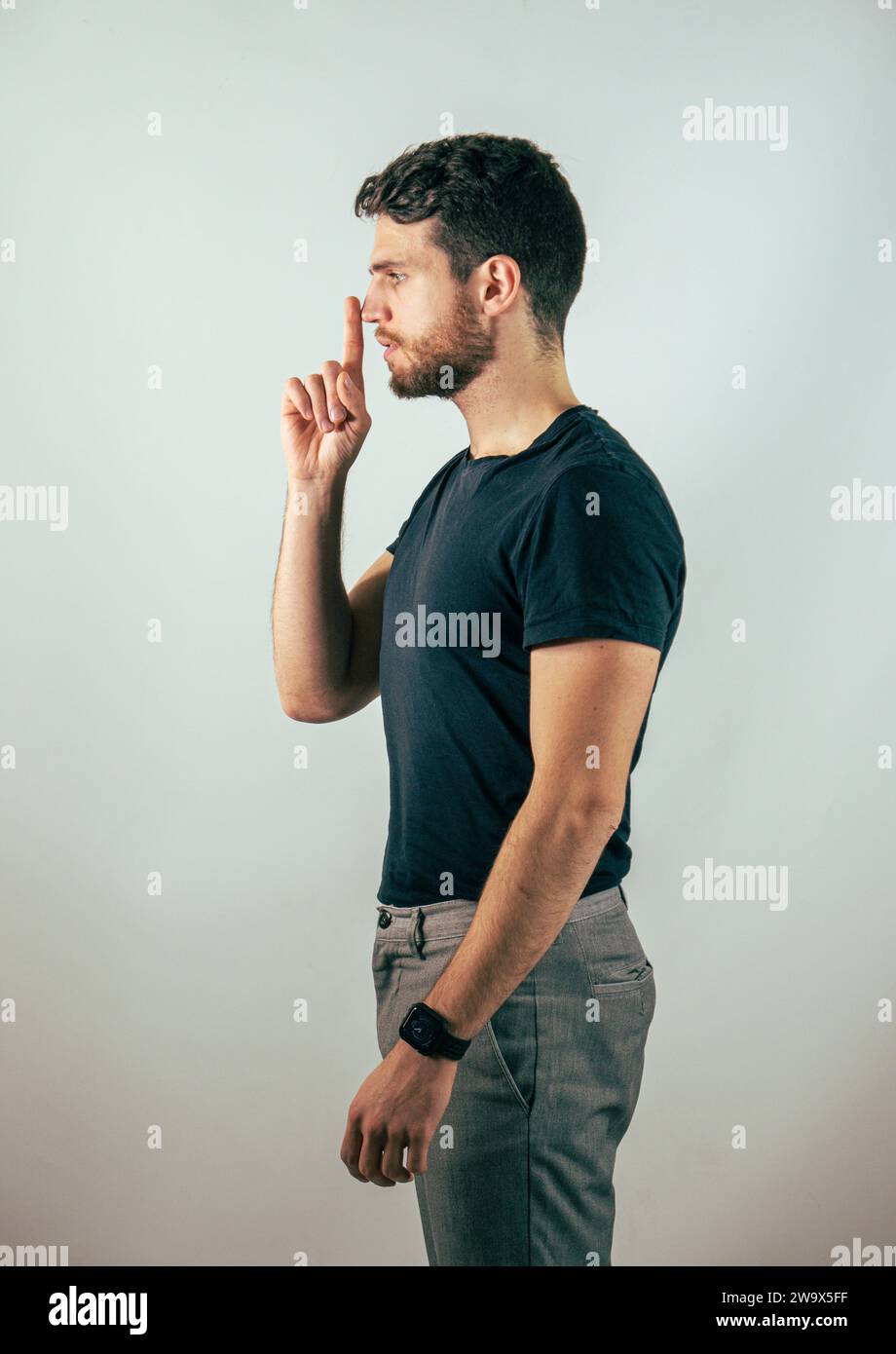 Hush. Young handsome man silencing you, saying shut up, in studio shot ...