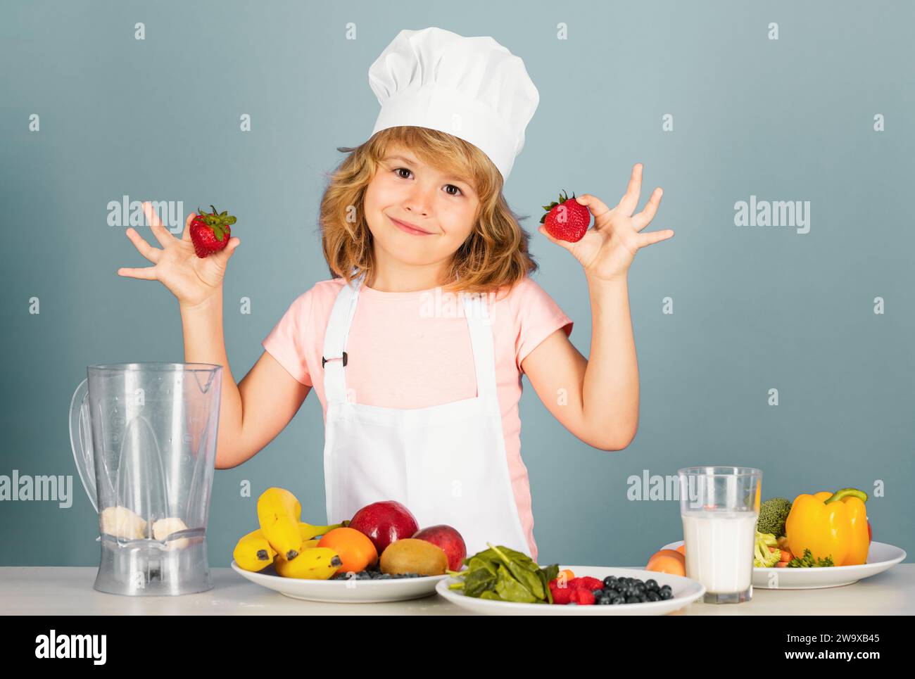 Child chef cook hold strawberries prepares food on isolated grey studio ...