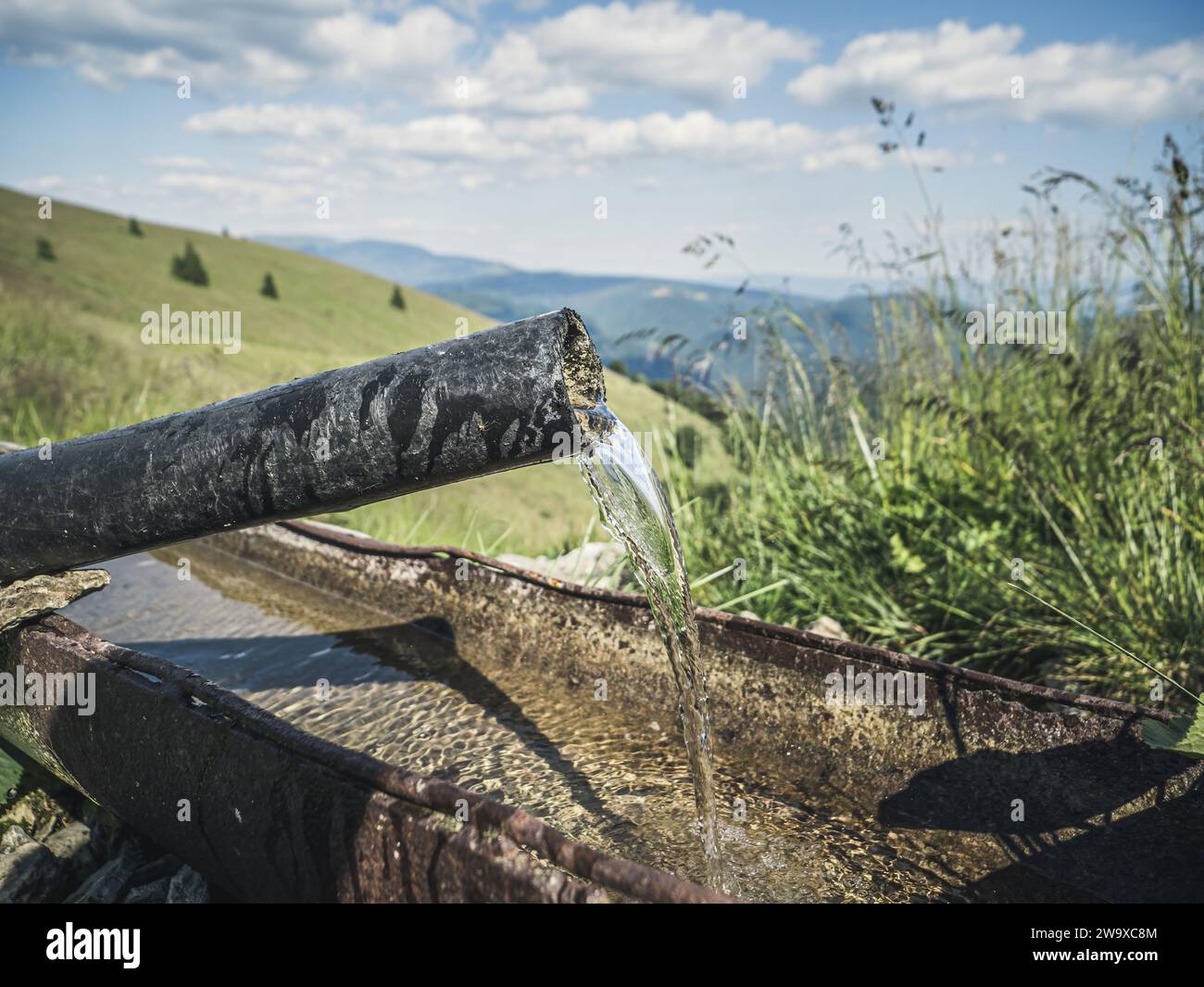 Water spring flowing from a tube with crystal clear mountain water in ...