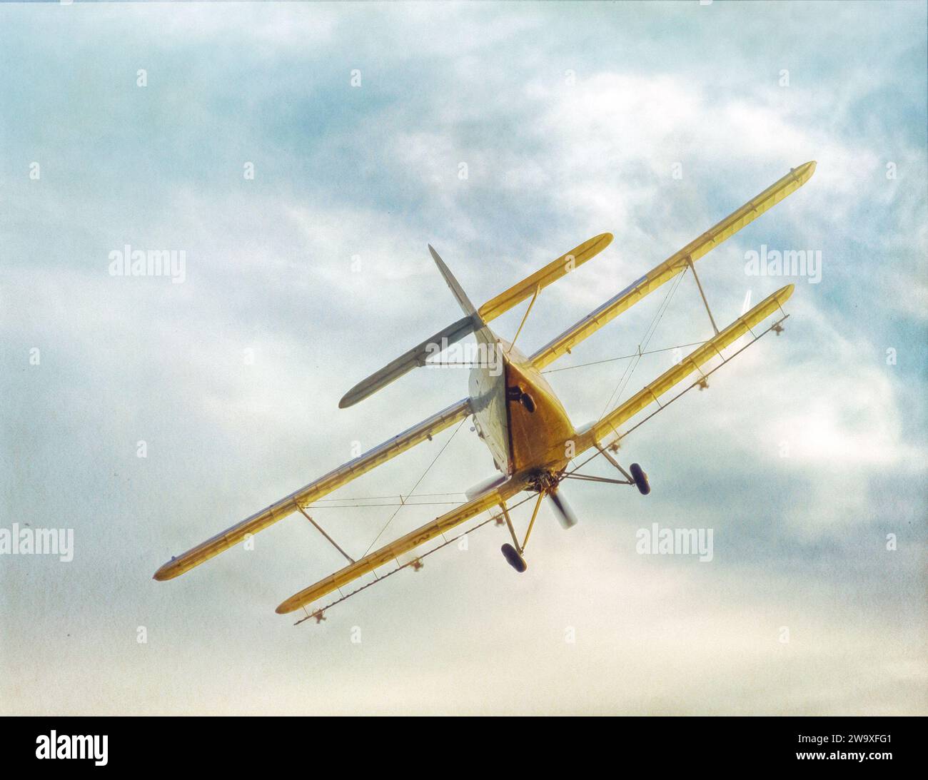 A yellow mosquito control plane flies across the sky, seen from behind ...
