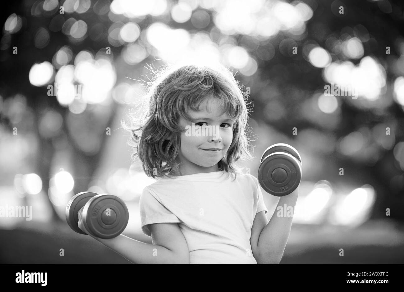 Fitness child. Portrait of sporty little boy with dumbbells in park ...