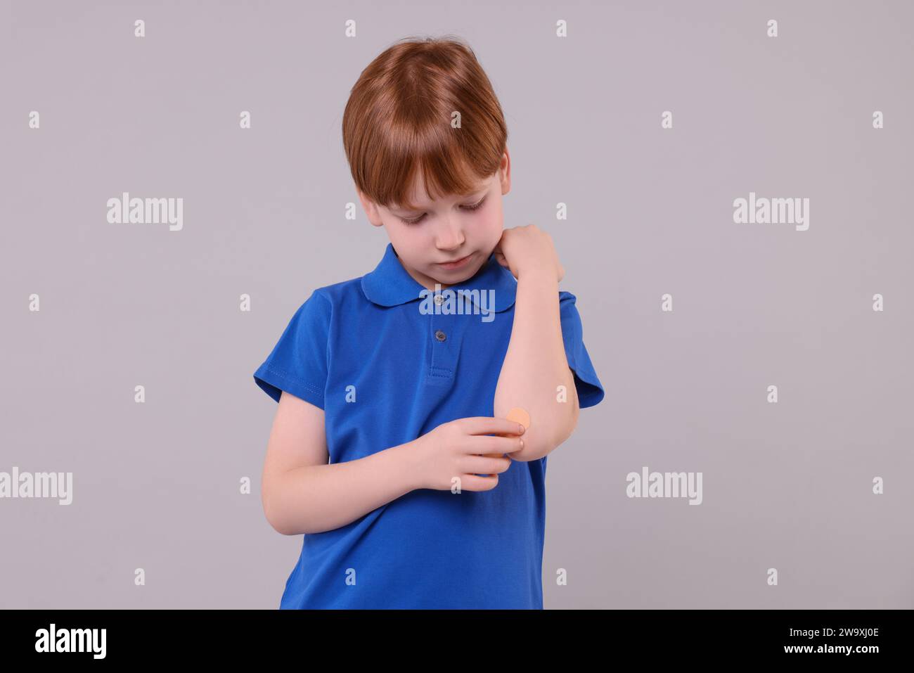 Little boy putting sticking plaster onto elbow against light grey ...