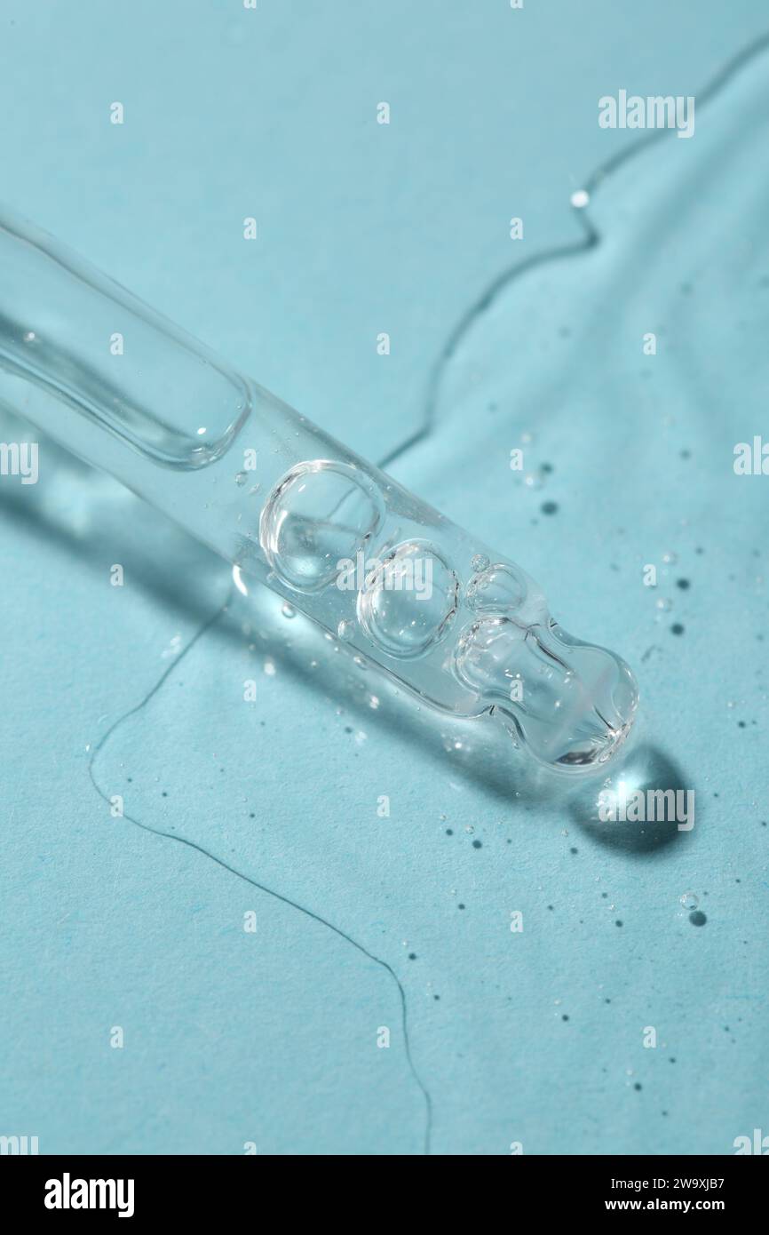 Dripping cosmetic serum from pipette onto light blue background, macro ...