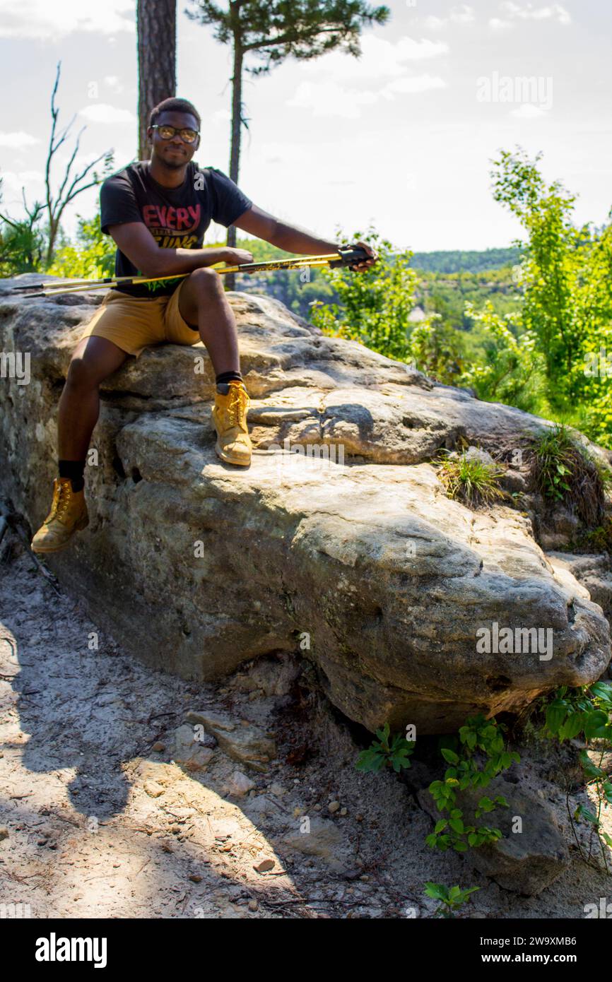 A portrait of an African male with hiking gear, sitting on a rock in ...