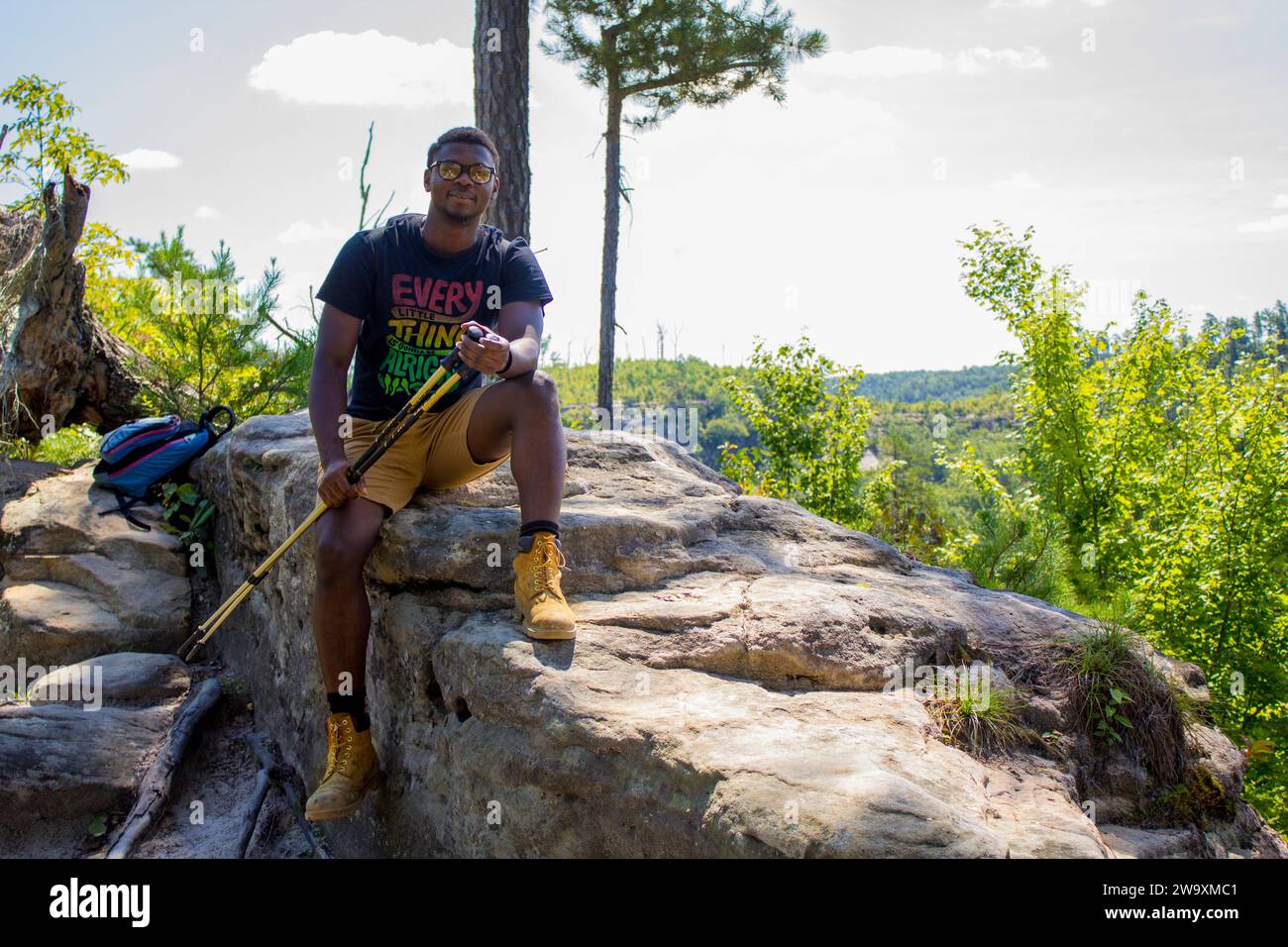 African male with hiking gear, sits on a rock in nature on a hiking ...