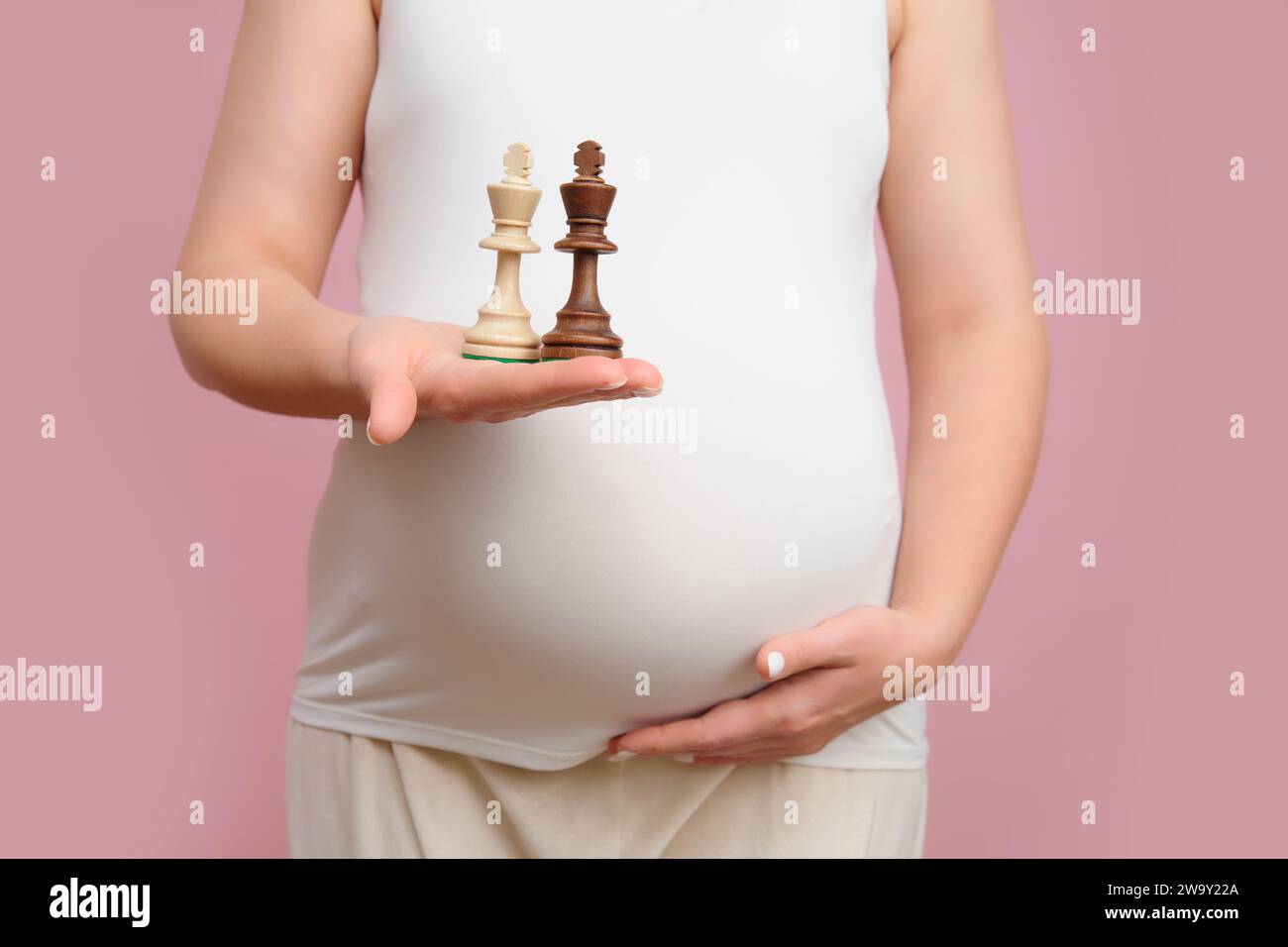 Pregnant woman holding chess pieces in her hand, studio pink background ...