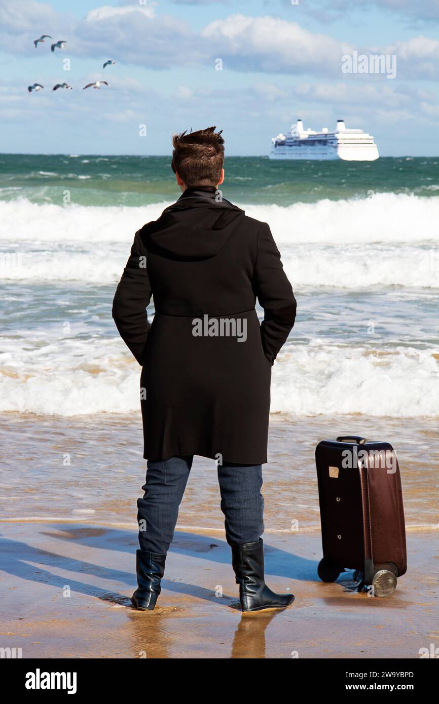 A young man in an overcoat with a travel case at his side, standing on ...