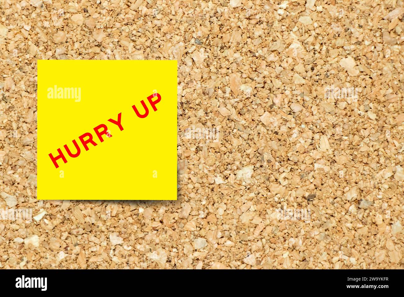 Yellow note paper with word hurry up on cork board background with copy ...
