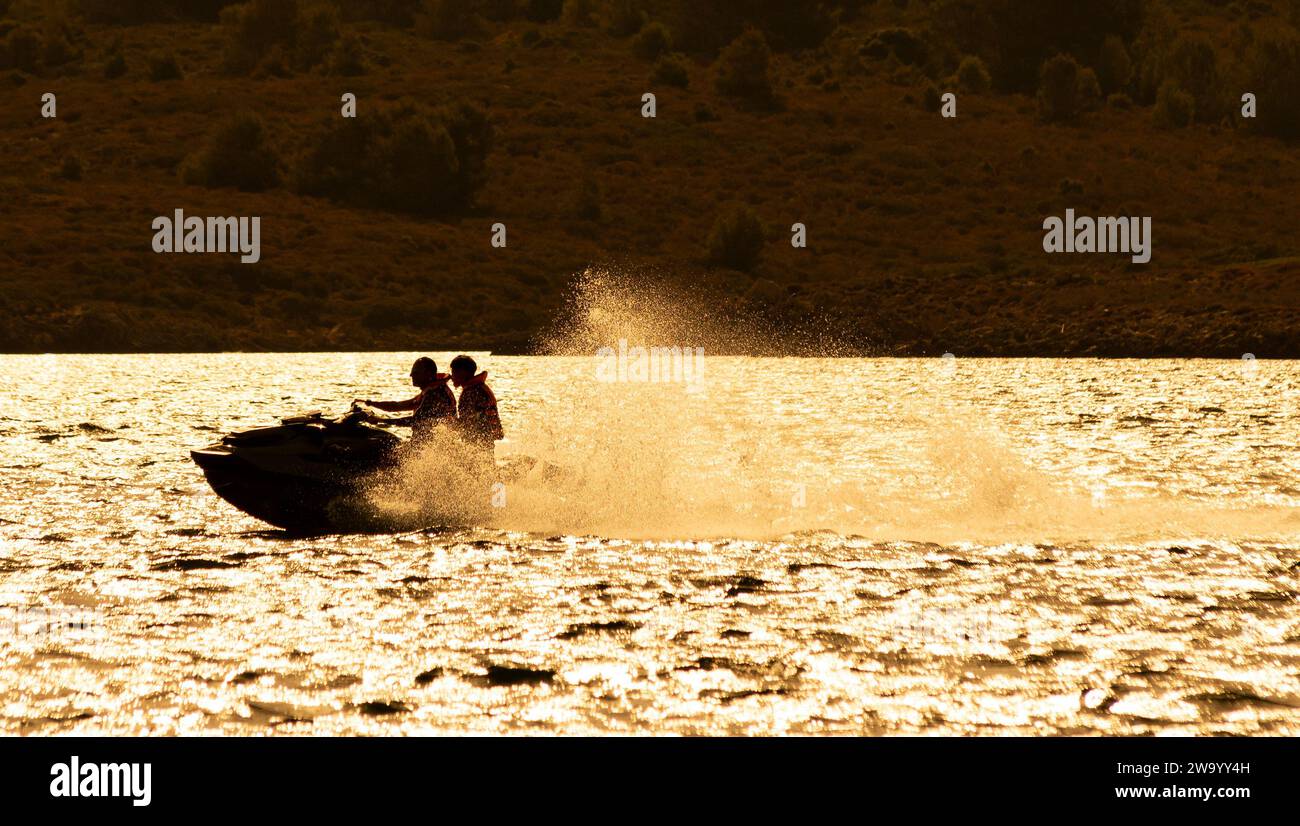 Two people riding a jet ski at speed in silhouette against the warm ...