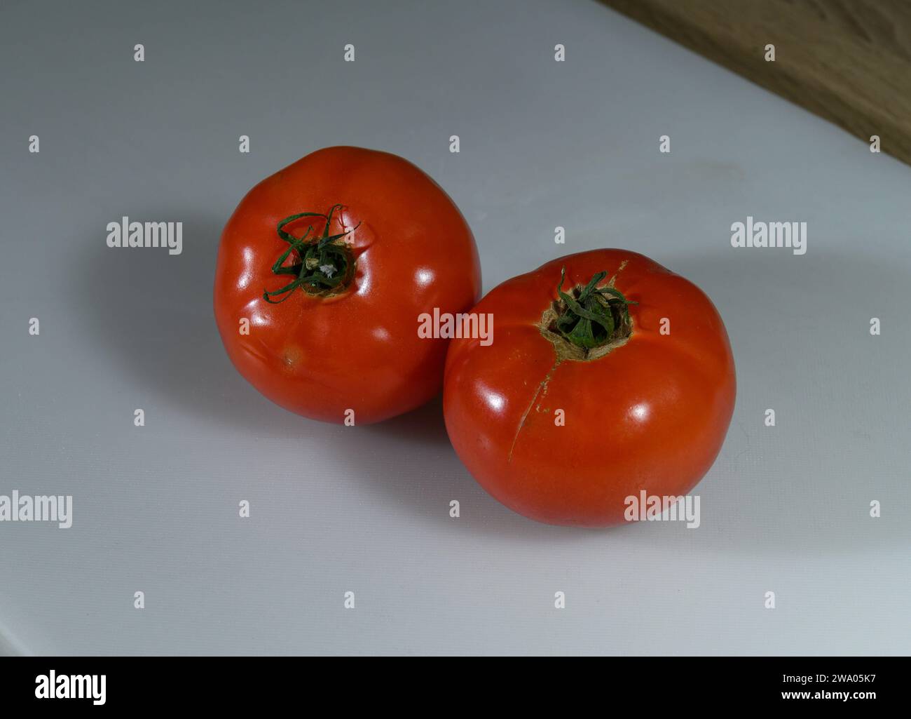 Close up of two whole raw tomatoes for salad on top of a white chopping ...