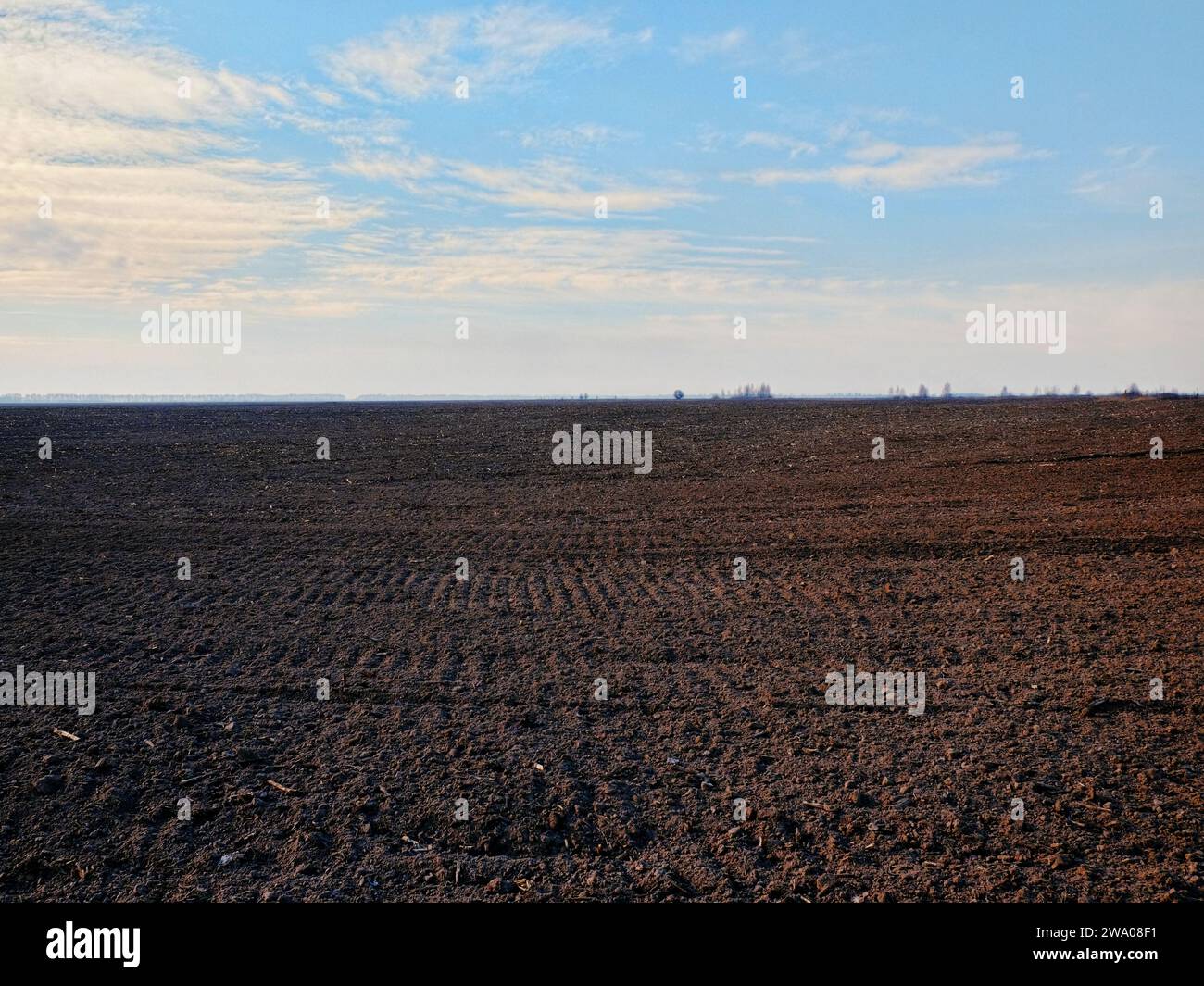 A vast field of plowed soil under a sky with scattered clouds Stock ...