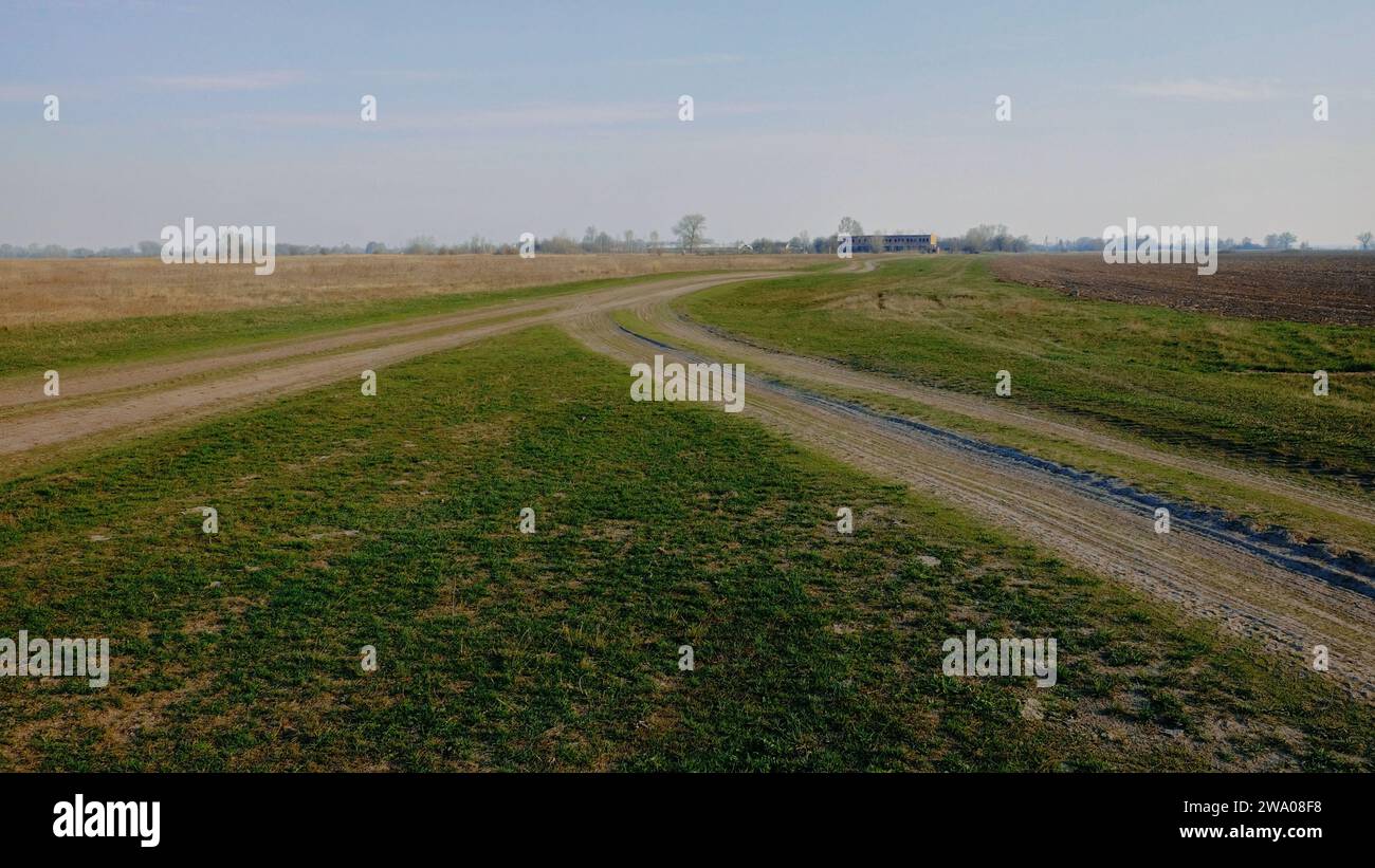 A clear sky overlooks an open field with a curving, tire-marked path ...