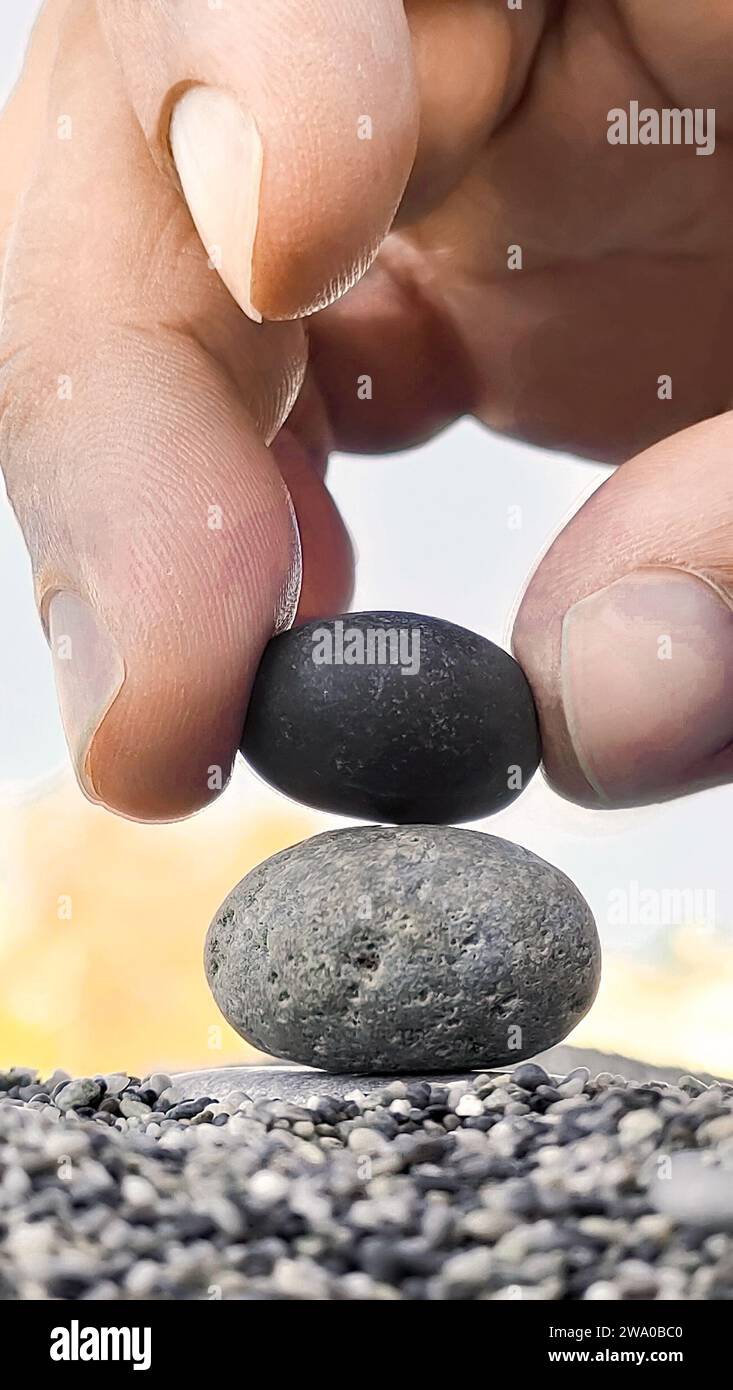 Hand of man places black stone on gray stone creating a pyramid, zen ...