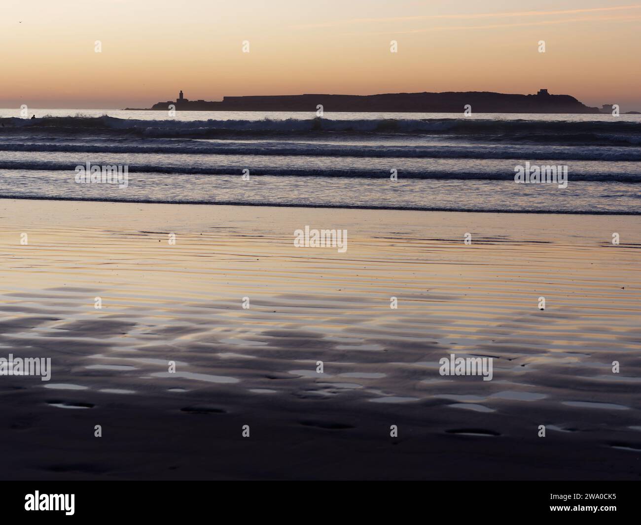 Sunset over an Island in Essaouira as waves roll towards a sandy beach ...
