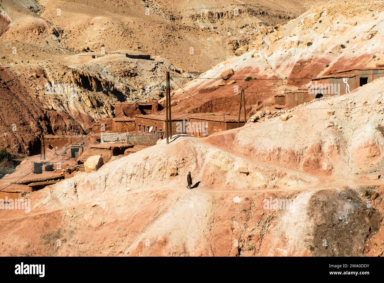 A lone man walks along a cliffside pathway outside a small village ...