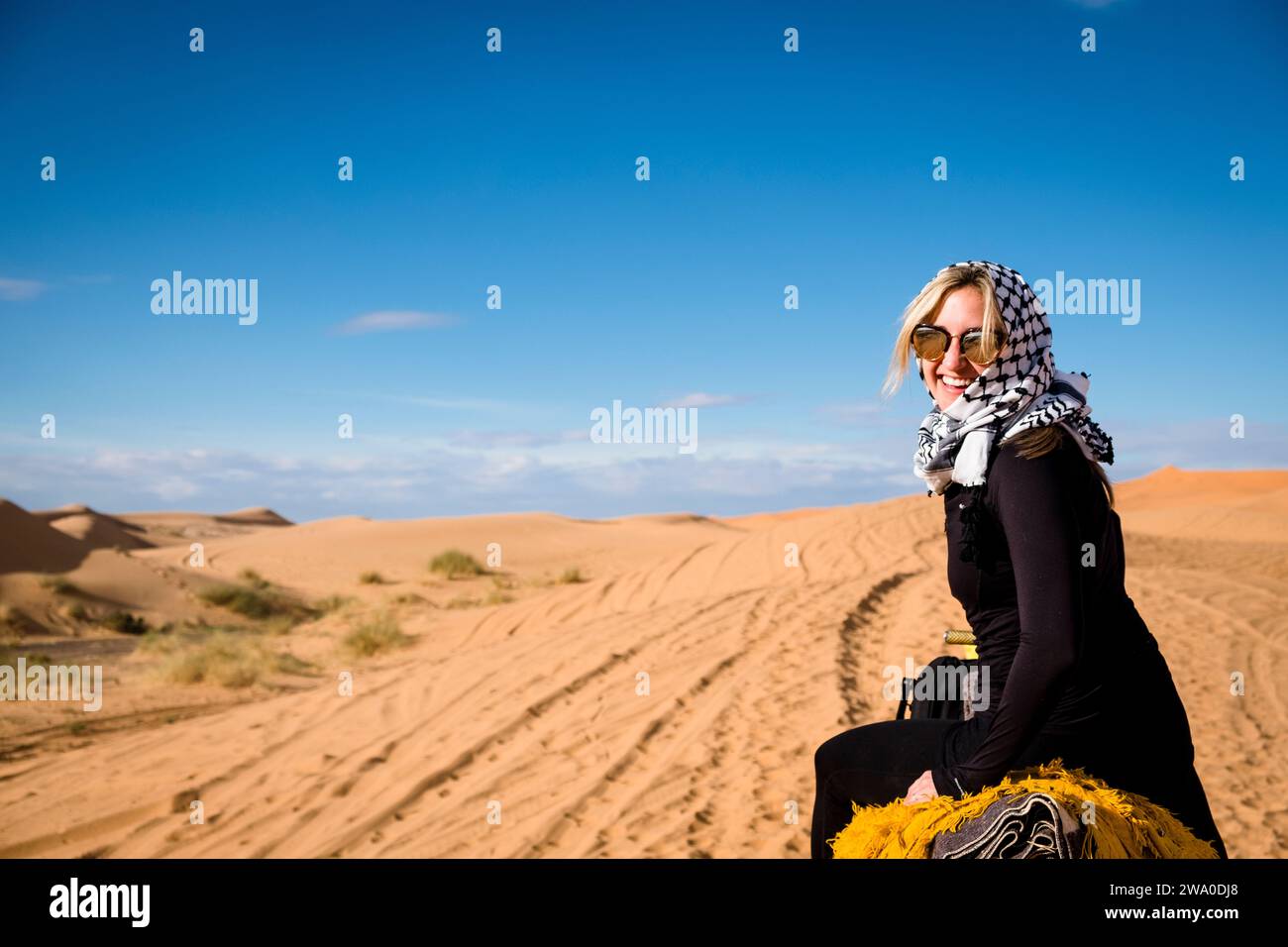 Female tourist on a camel turns to look at the camera while trekking ...