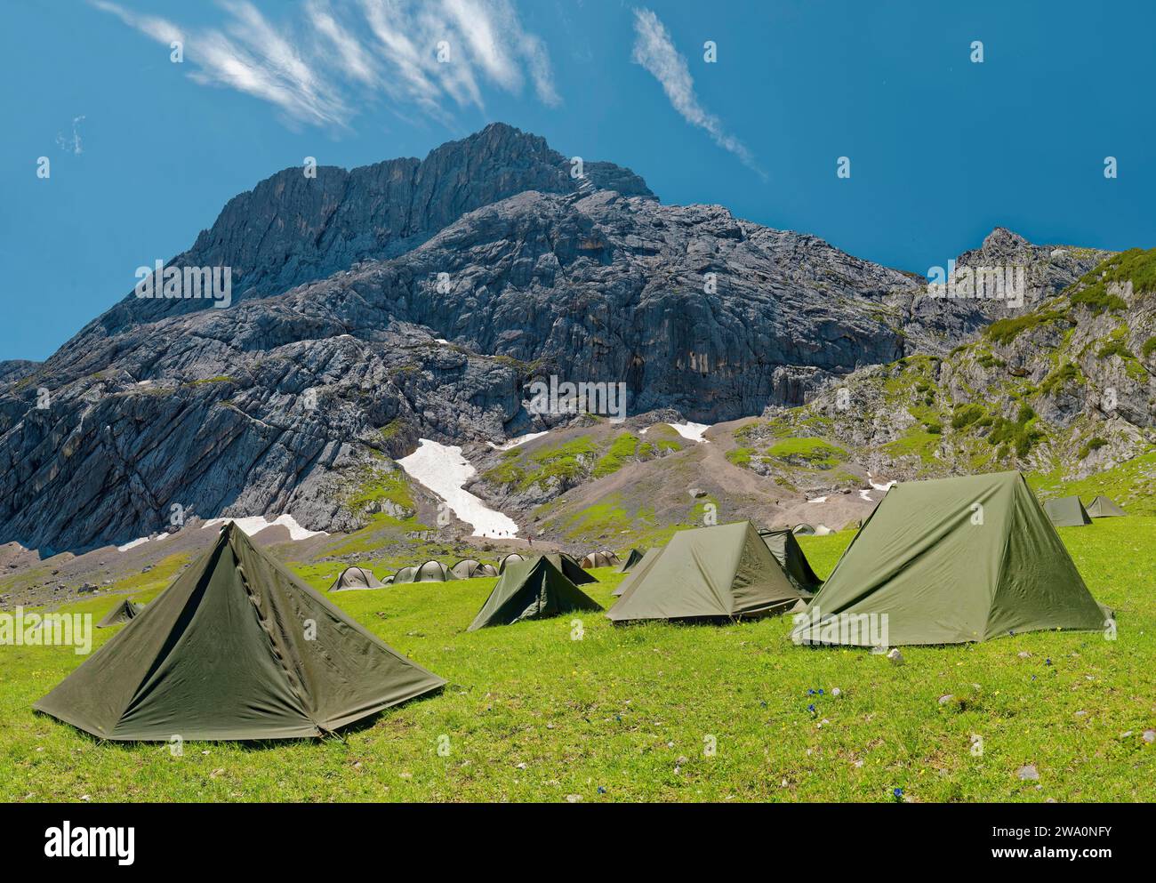 Tents of mountain hunters on a green meadow in front of an imposing ...