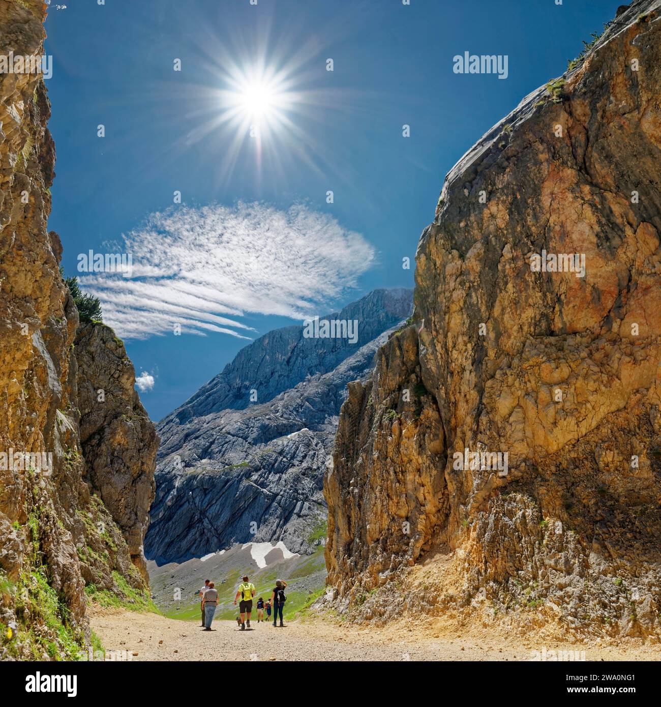 A group of hikers between imposing rock faces under a bright blue sky ...