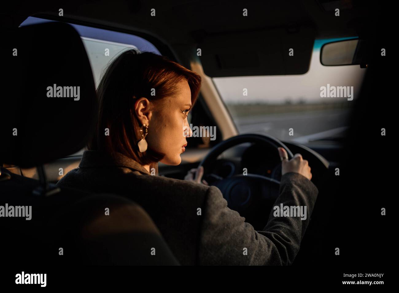 Young beautiful smiling woman taxi driver in a jacket sits behind the ...