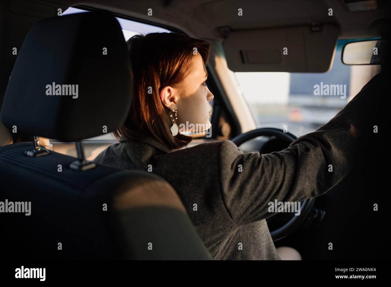 Young beautiful smiling woman taxi driver in a jacket sits behind the ...