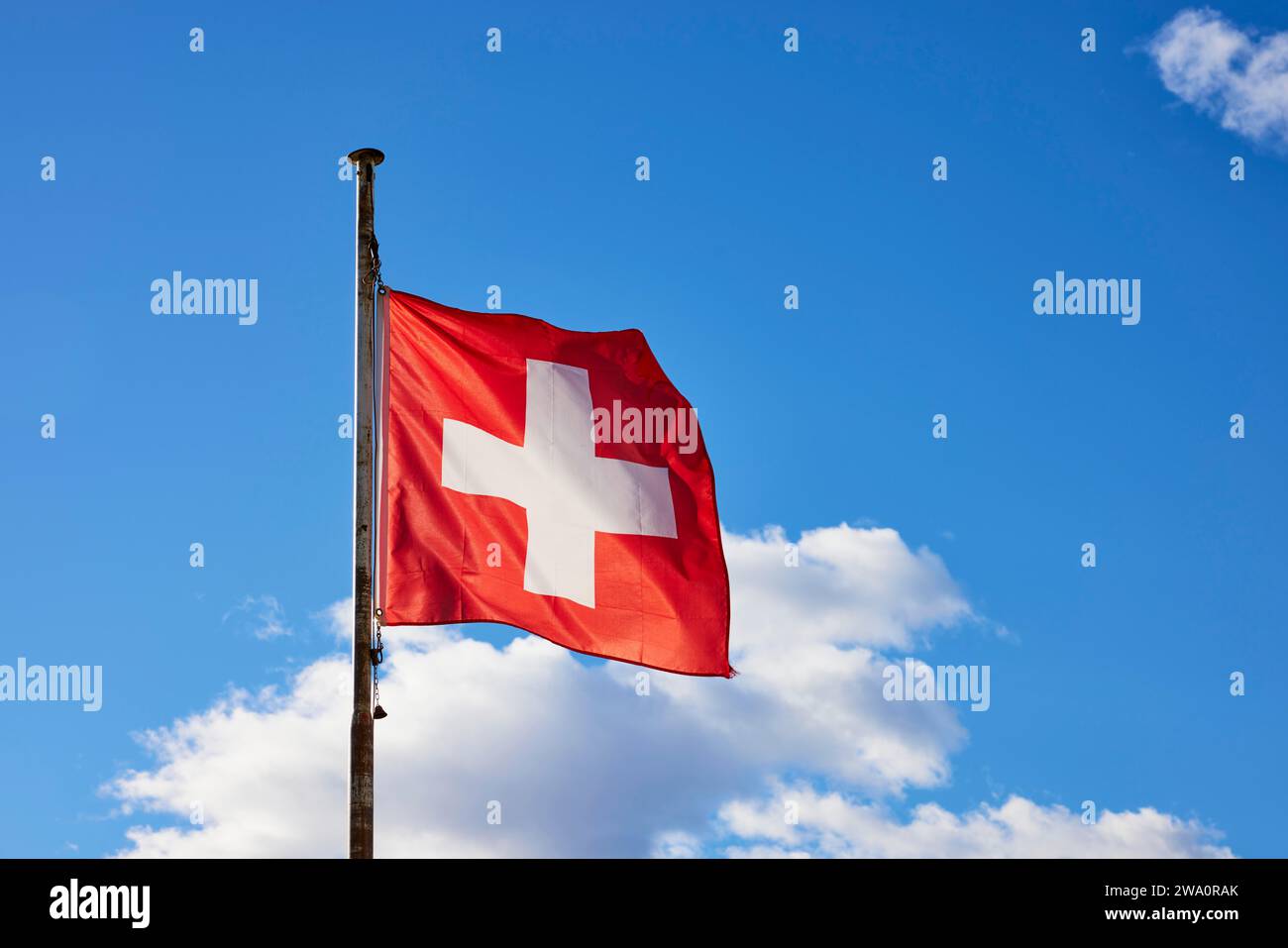 Swiss flag on a flagpole in front of a blue sky with white clouds in ...