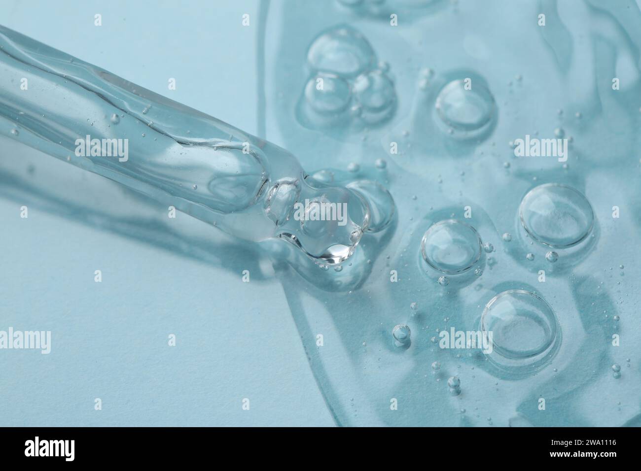 Dripping cosmetic serum from pipette onto light blue background, macro ...