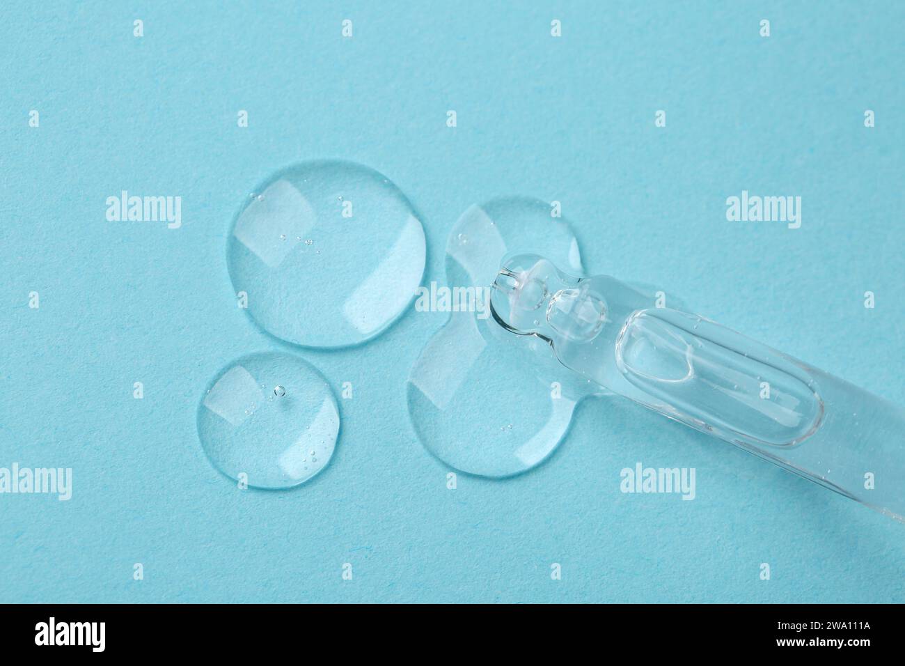 Dripping cosmetic serum from pipette onto light blue background, top ...