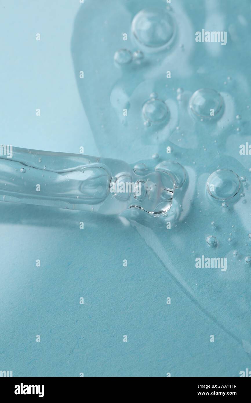 Dripping cosmetic serum from pipette onto light blue background, macro ...