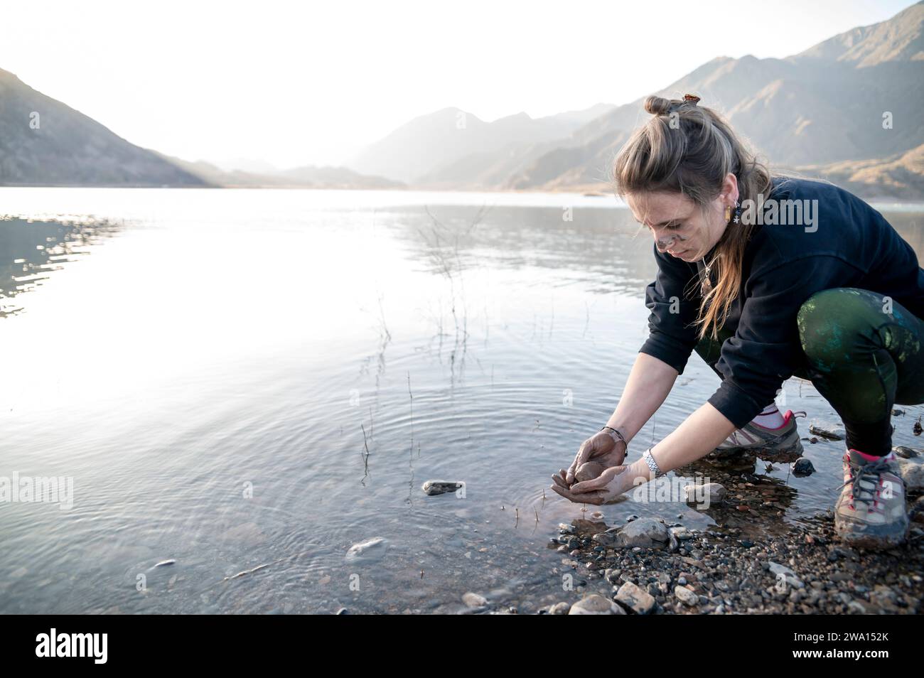 Woman putting mud on hands and face while enjoying outdoors in nature ...