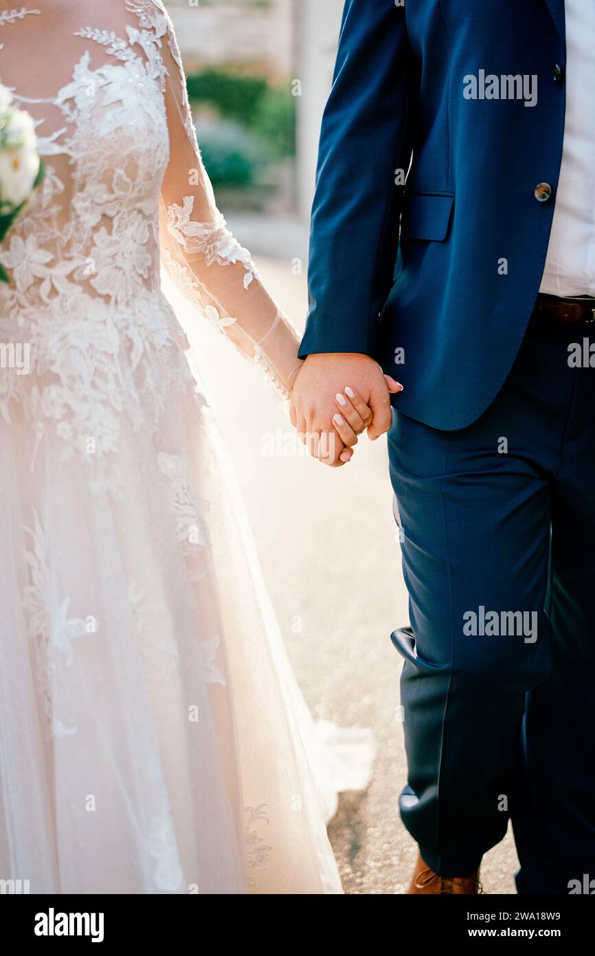 Bride and groom are walking holding hands along the road. Cropped ...