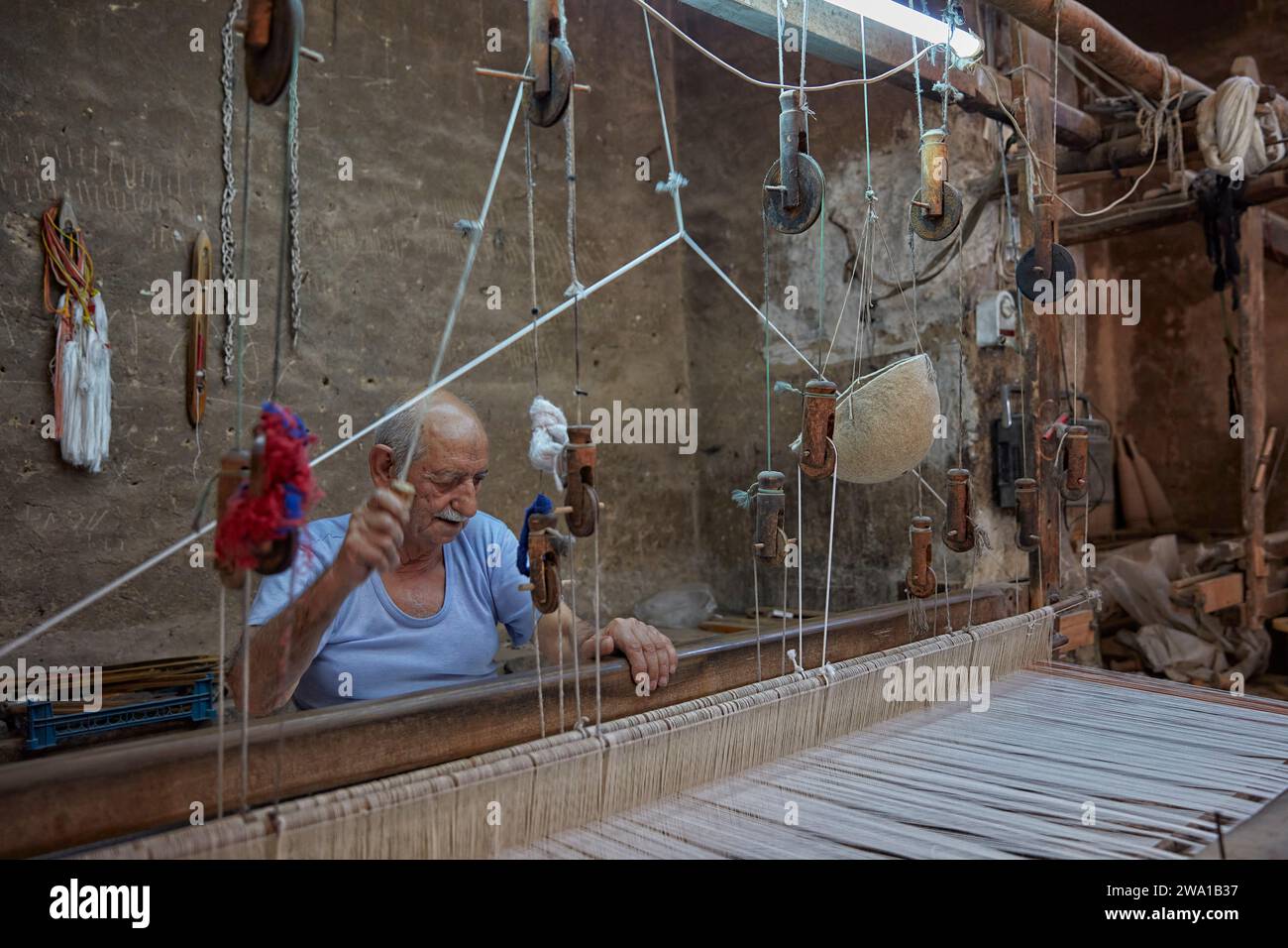 An older man works on horizontal loom in weaving workshop. Kashan, Iran ...