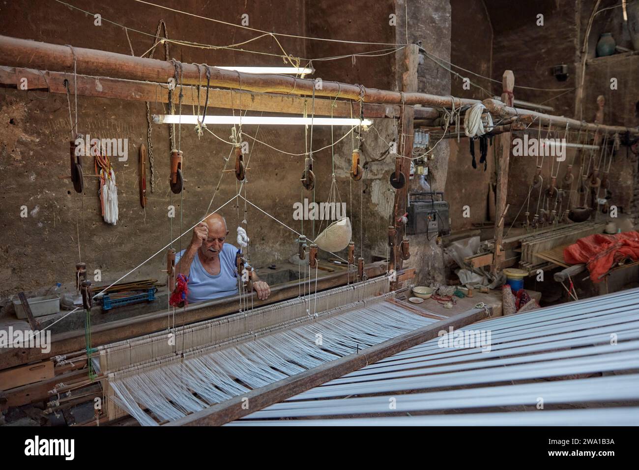 An older man works on horizontal loom in weaving workshop. Kashan, Iran ...